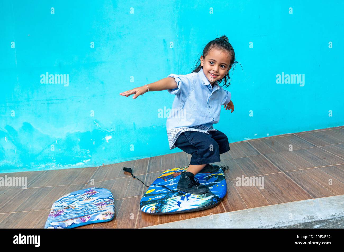 A cute boy with long hair practicing surfing in different poses at home ...