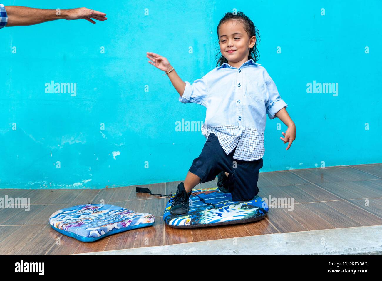 A cute boy with long hair practicing surfing in different poses at home ...
