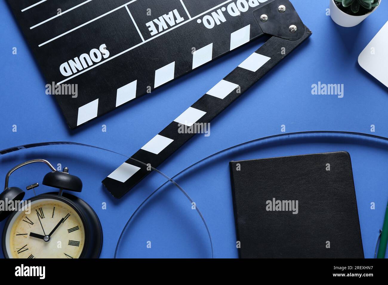 Notebook with movie clapper, film reel and alarm clock on blue ...