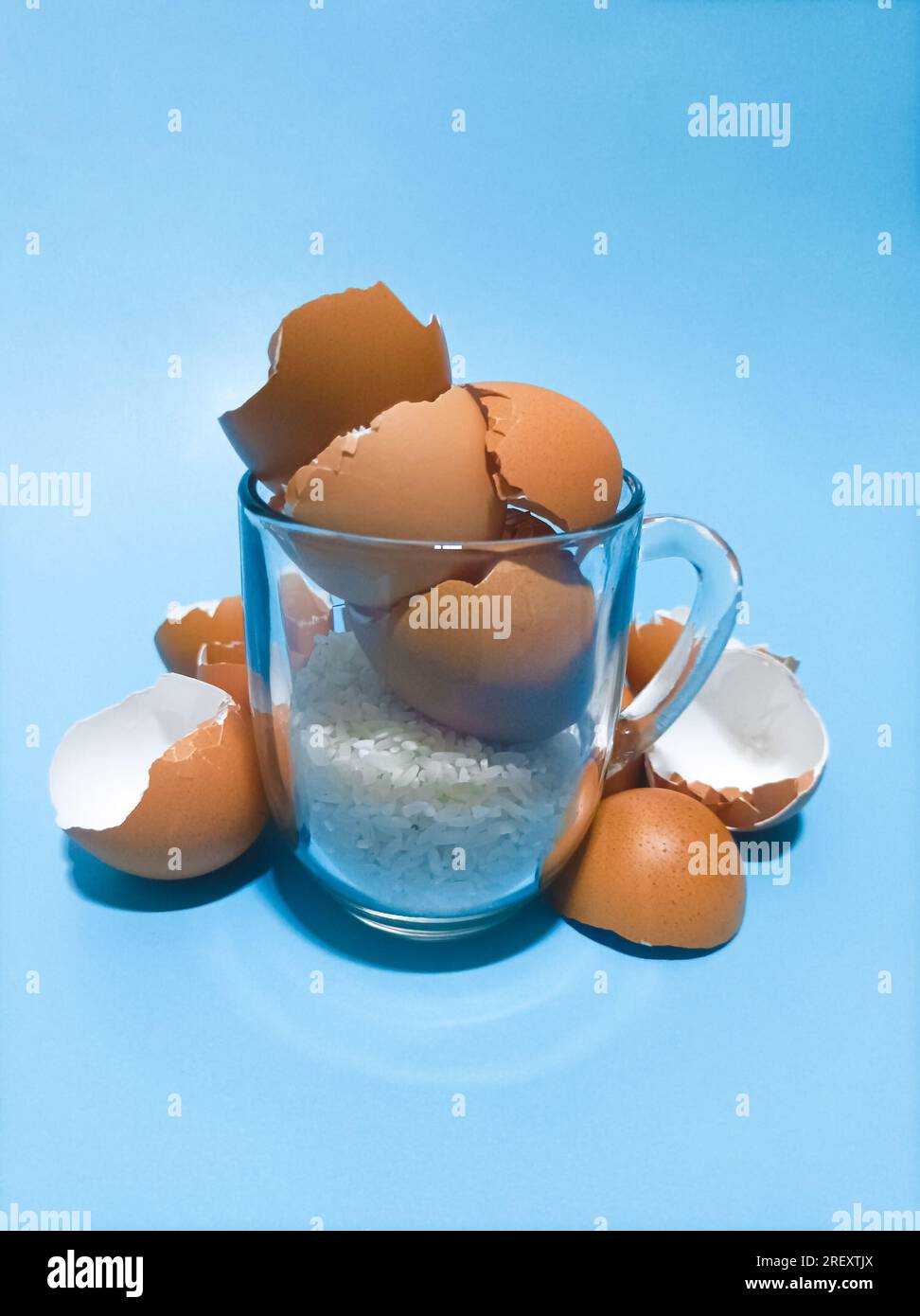Egg shells and raw rice in a glass cup on a blue background. Kitchen ...