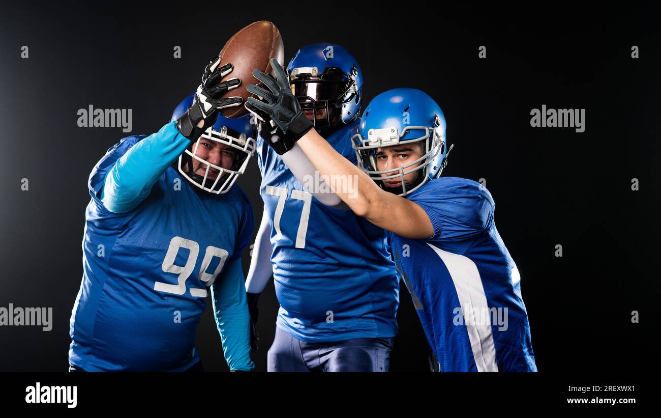 Three American football players raising their hands up holding the ball ...