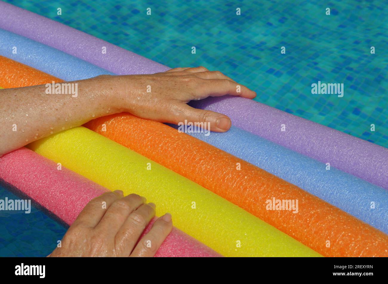 Rainbow coloured floating foam sticks and female hands, in swimming ...