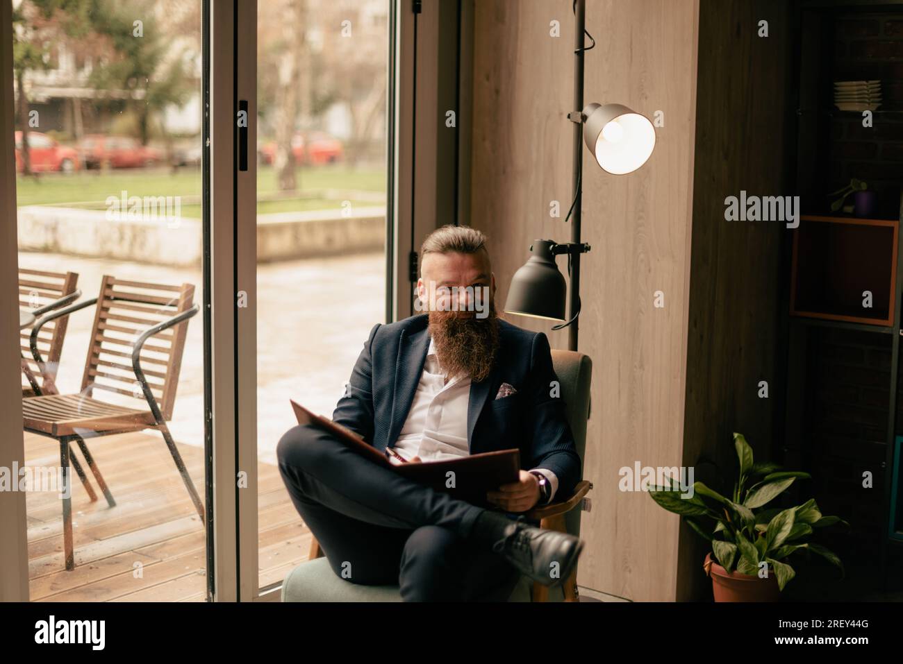 Handsome bearded man writing something on his notepad with his legs ...