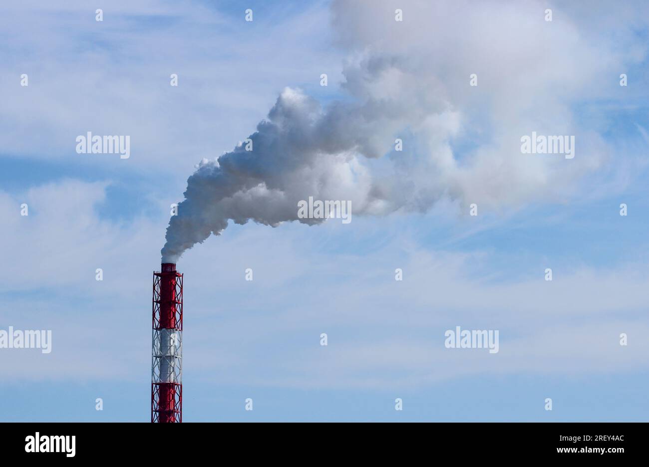 Thick smoke from an industrial pipe against a blue sky with clouds ...