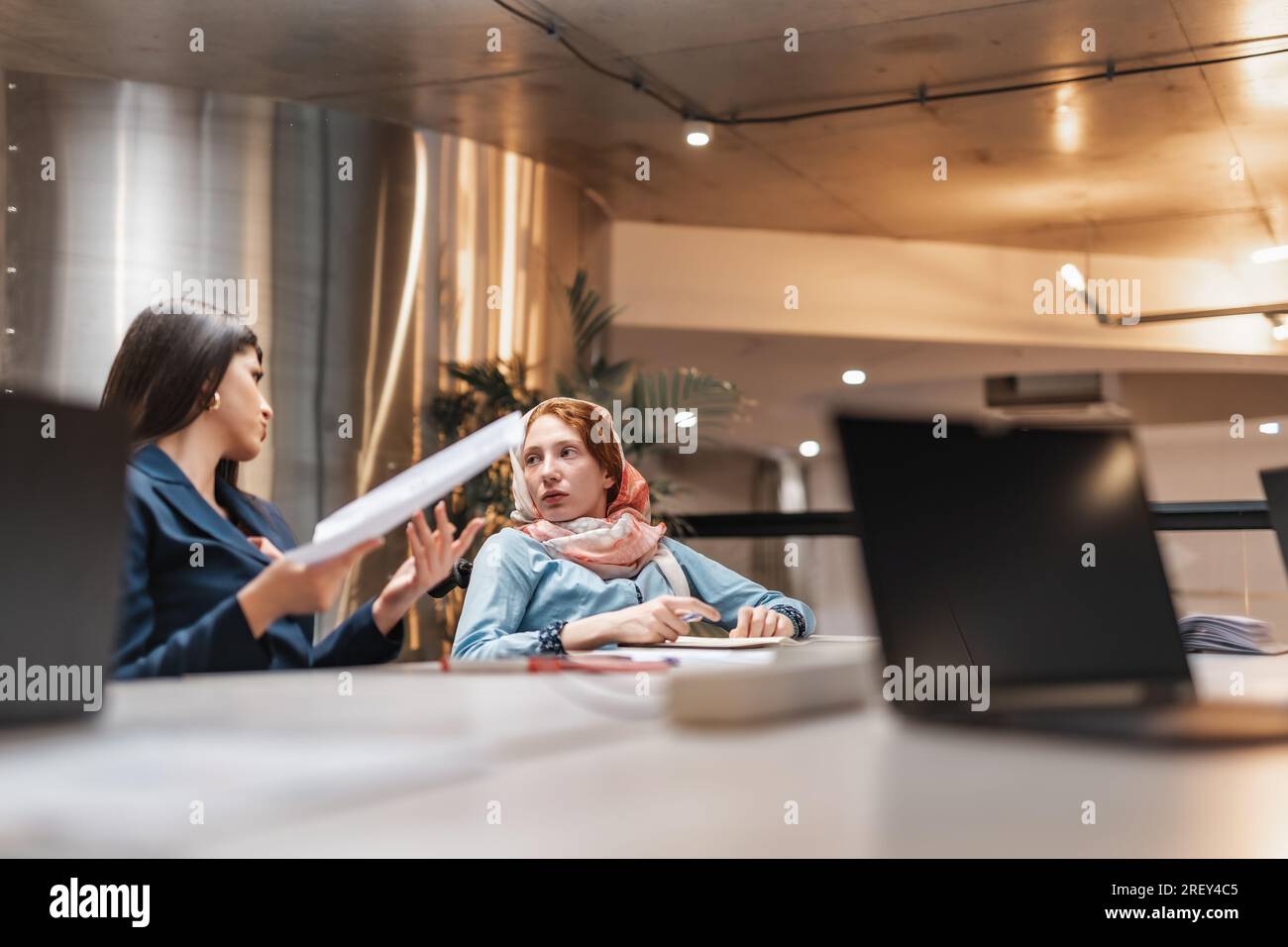 Muslim female ginger employee listening to her brunette colleague ...