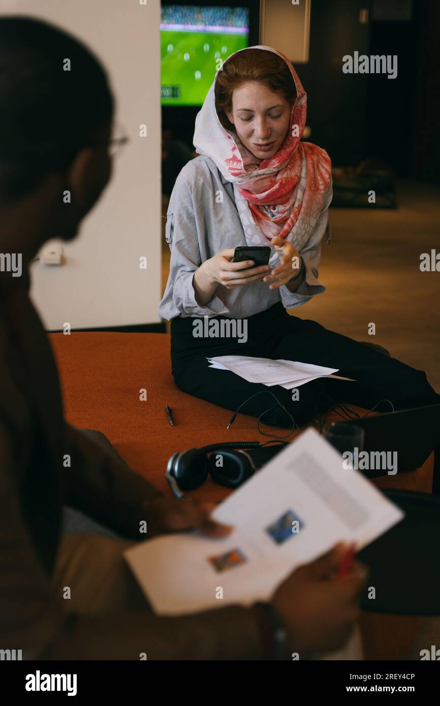 Gorgeous ginger muslim employee checking her phone while having a ...