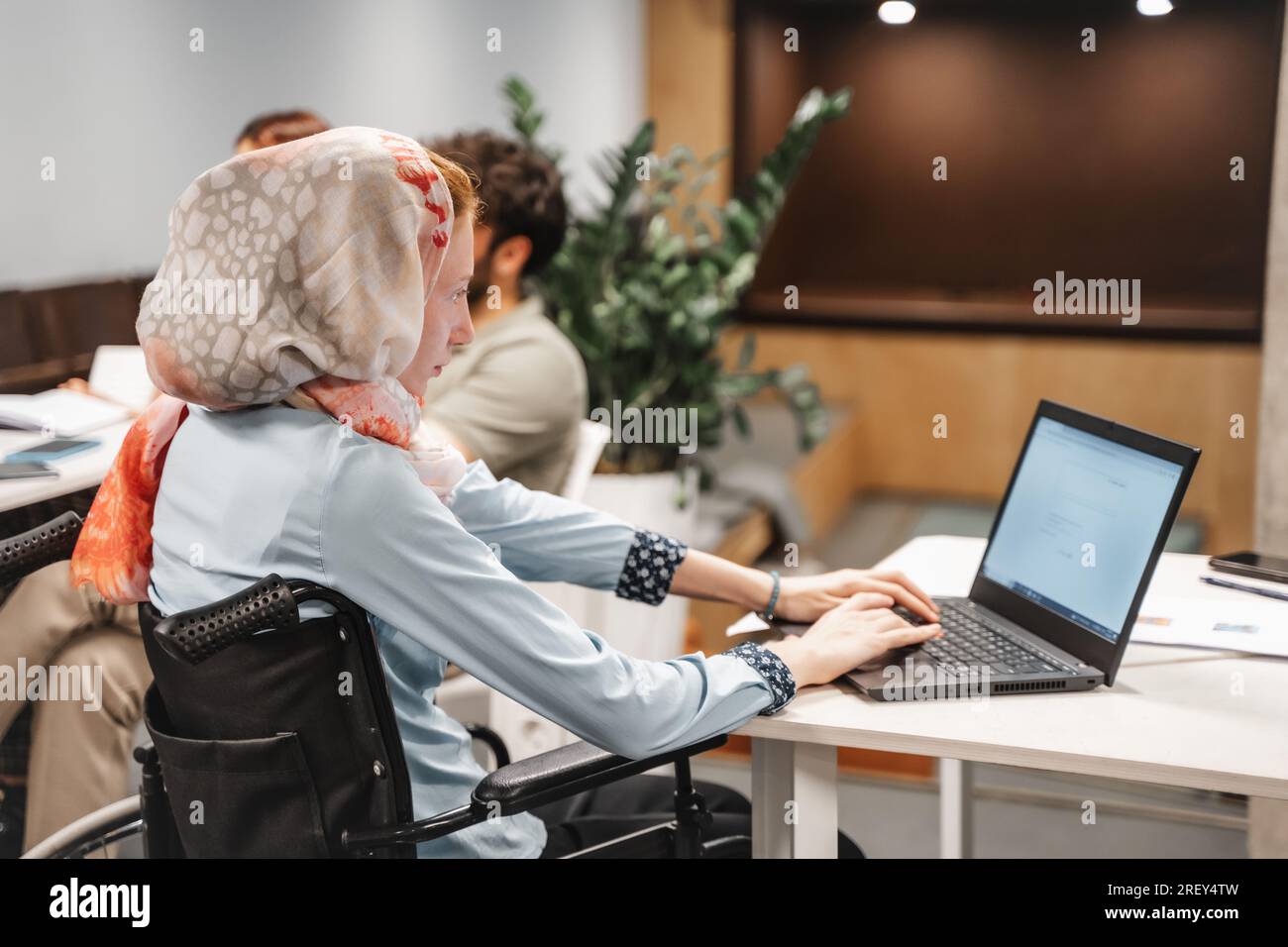 Disabled female employee in wheelchair working on a lap top. Side photo ...