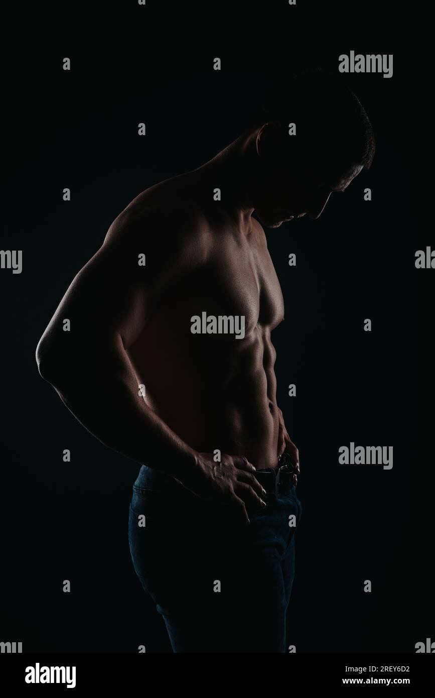 Stunning and well-built man standing in a dark room and flexing his ...