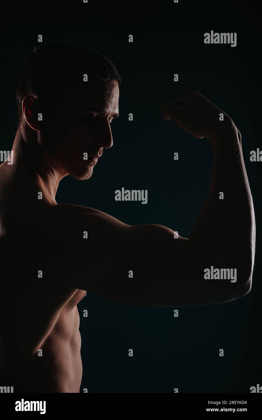 Muscular and good-looking man standing in a dark room and flexing his ...