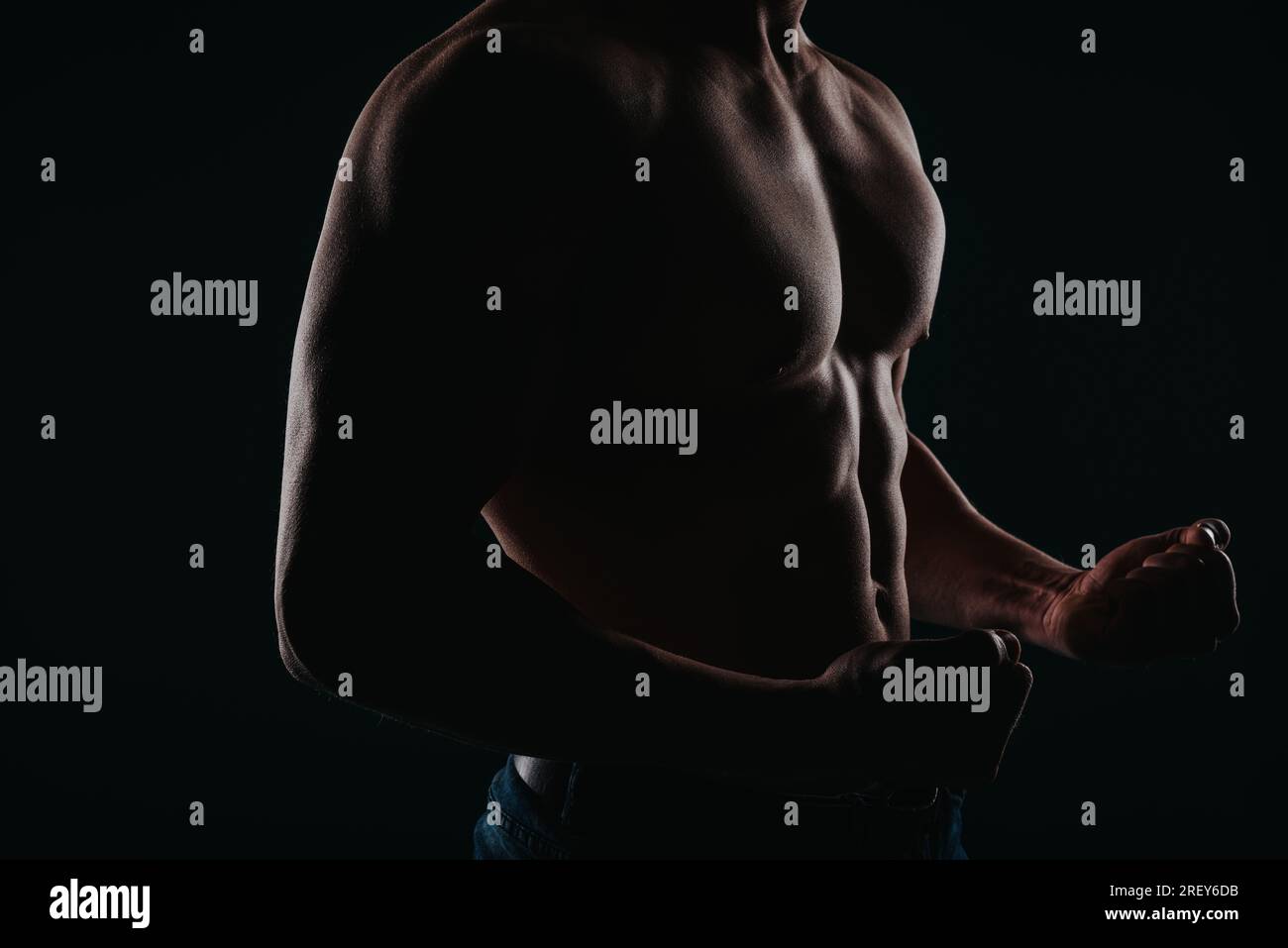 Stunning and well-built man standing in a dark room and flexing his ...