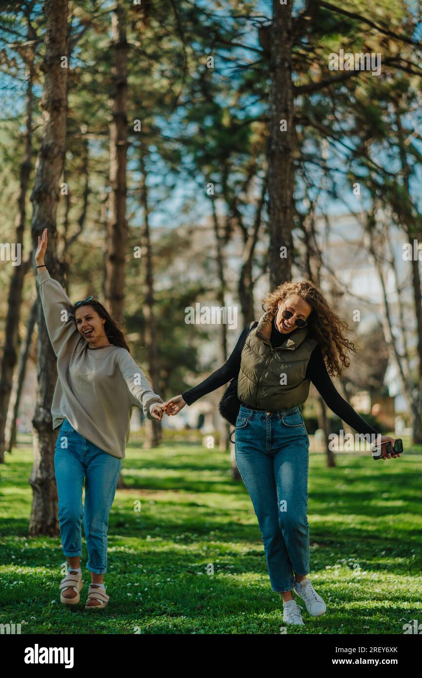 Two smiley, gorgeous girls spreading arms while walking in the park ...