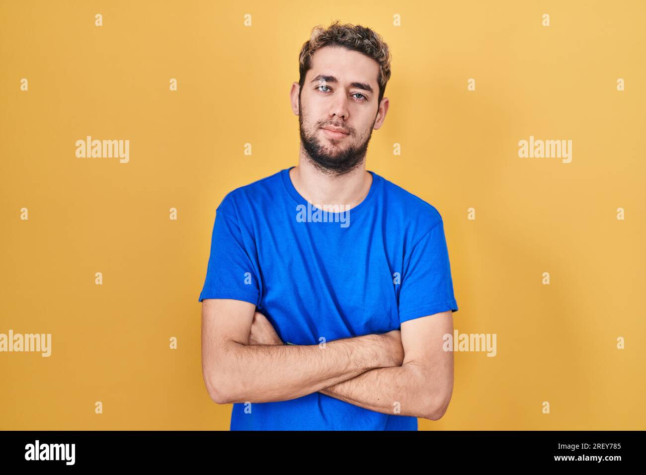 Hispanic man with beard standing over yellow background looking sleepy ...
