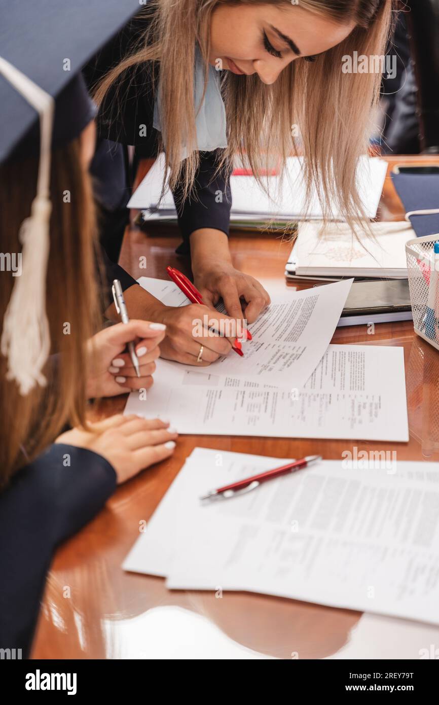 Two young and beautiful university graduates writing and signing ...