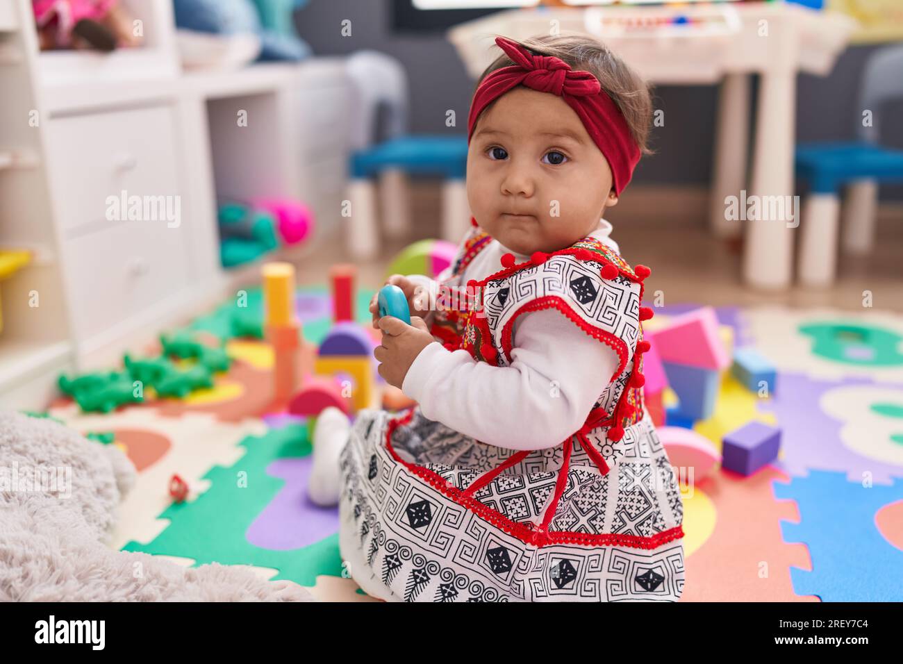 Adorable hispanic baby sitting on floor with relaxed expression at ...