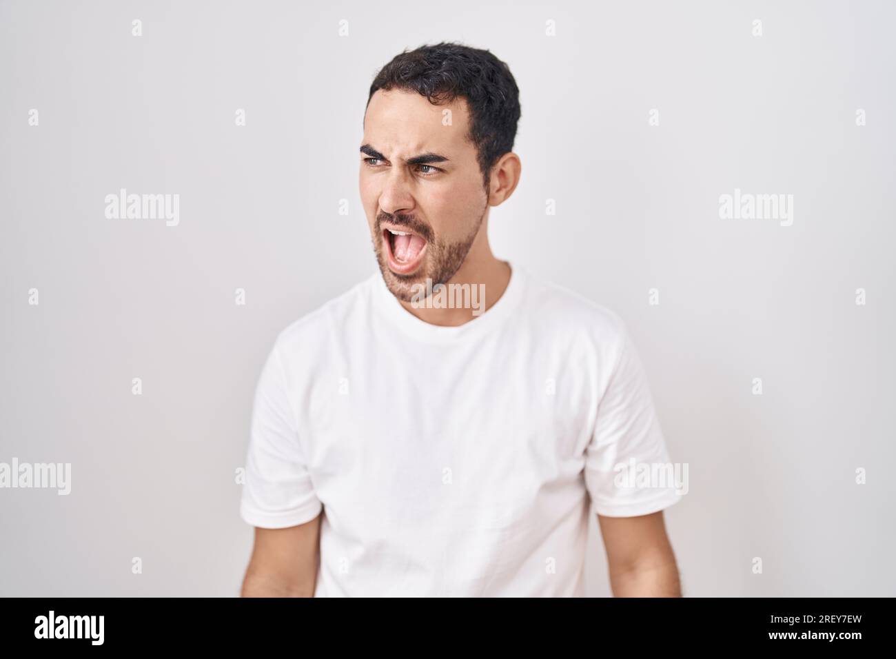 Handsome hispanic man standing over white background angry and mad ...