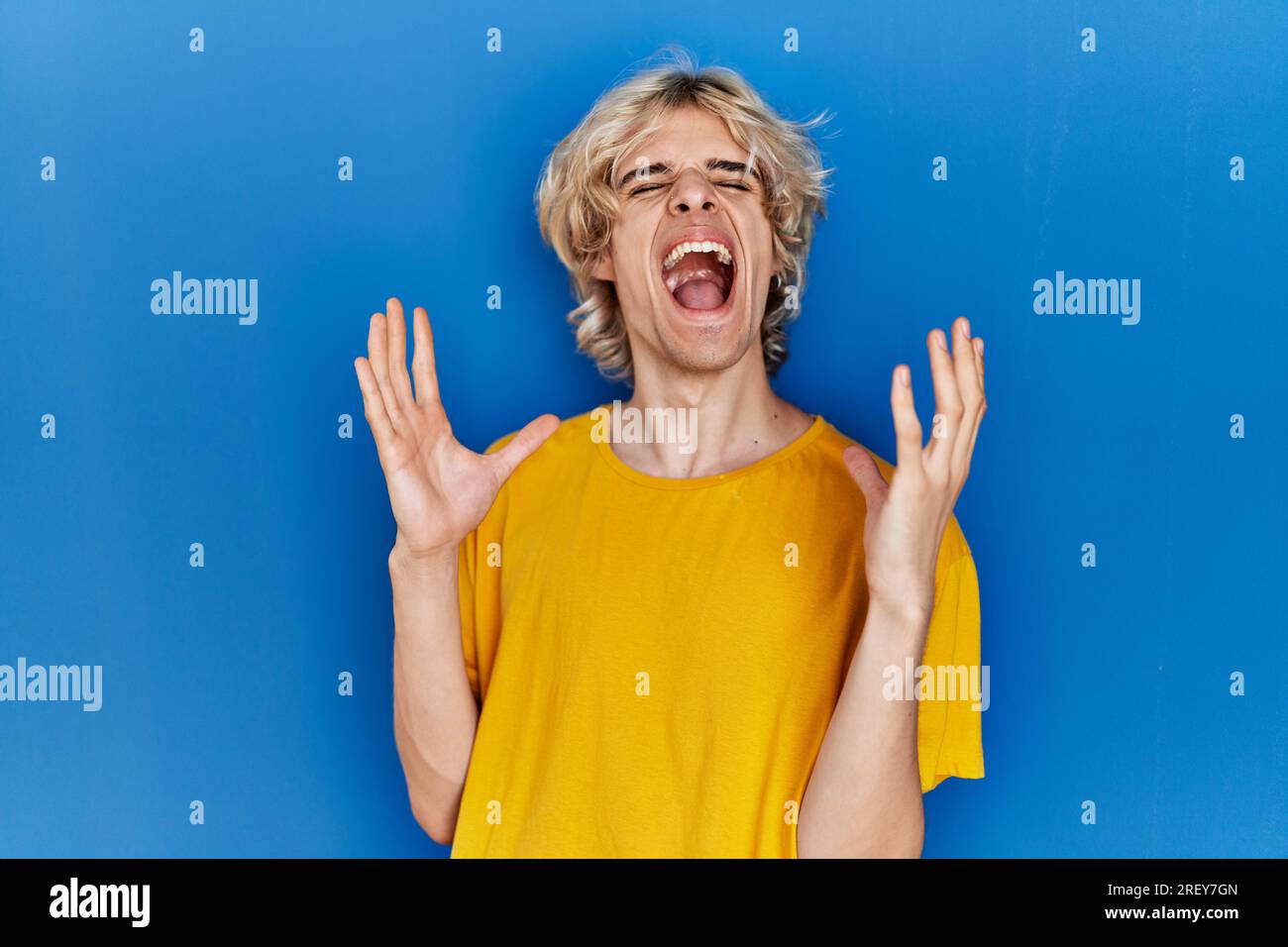 Young modern man standing over blue background celebrating mad and ...