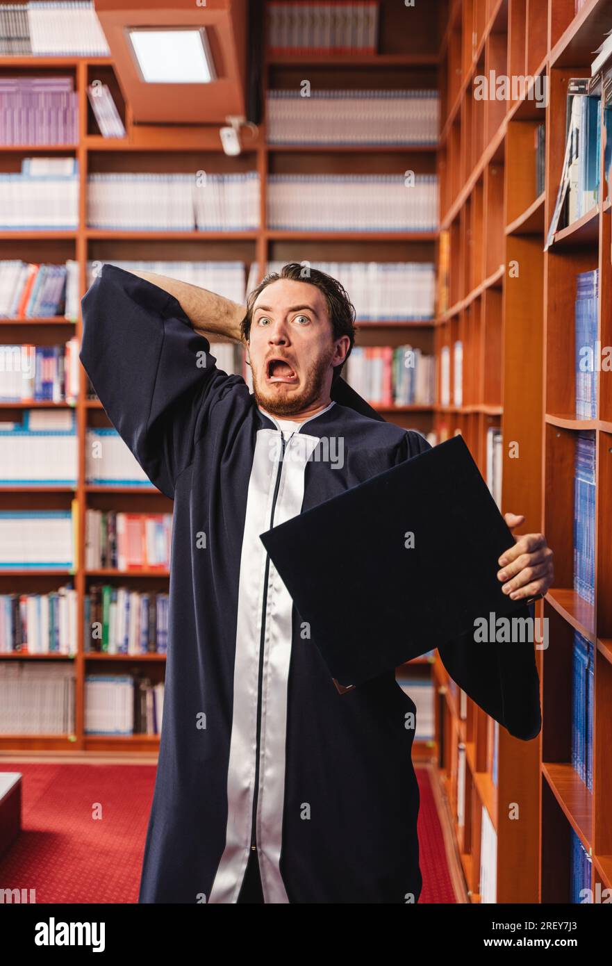 Young graduate wearing a gown shocked while holding his university ...