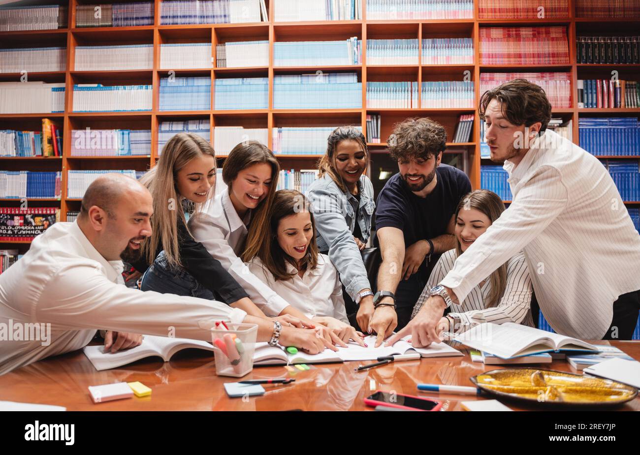 Young group of students pointing at a book while working on a project ...