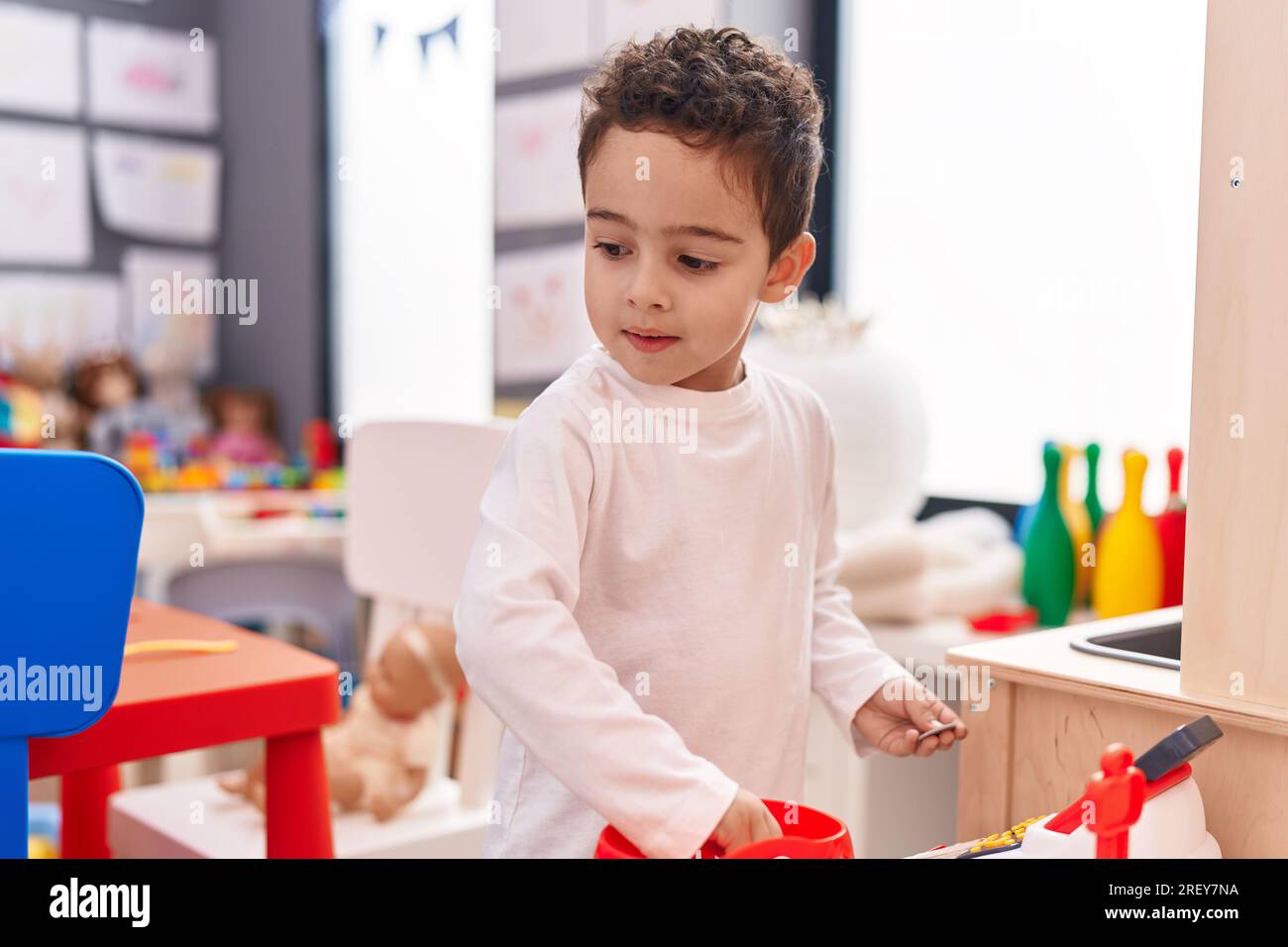 Adorable hispanic boy playing supermarket game standing at kindergarten ...