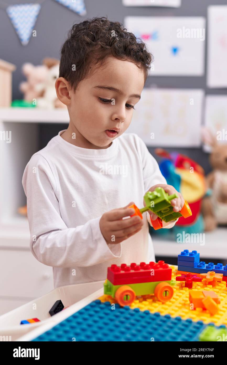 Adorable hispanic boy playing with construction blocks standing at ...