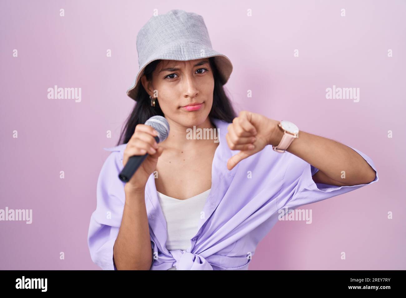 Young hispanic woman singing song using microphone over pink background ...