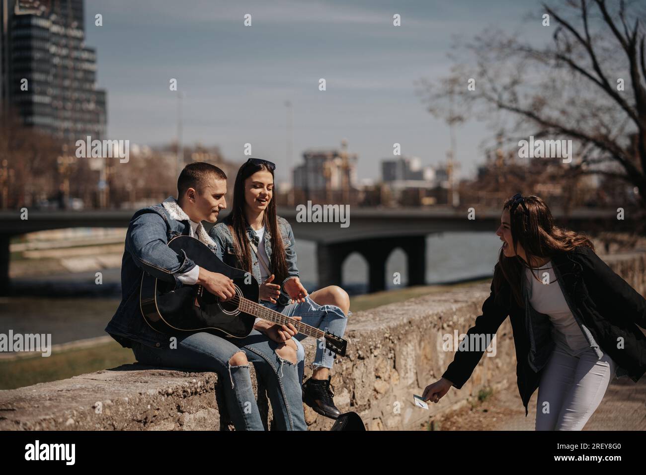 Beautiful couple playing guitar and singing while sitting at the river ...