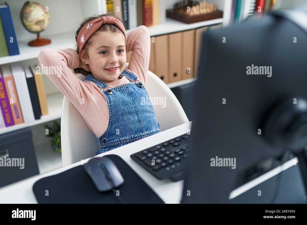 Adorable hispanic girl student using computer relaxed with hands on ...