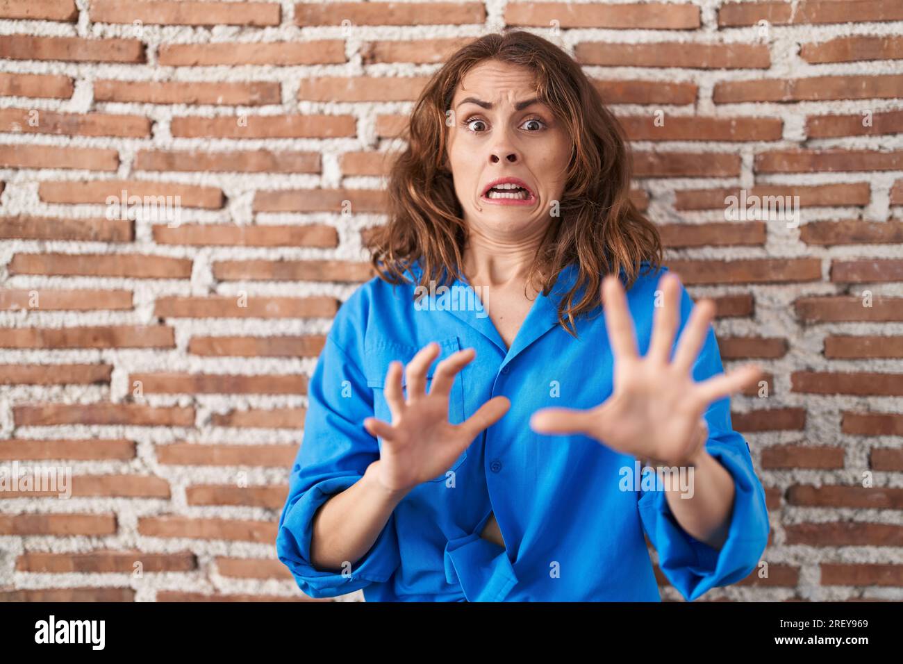 Beautiful brunette woman standing over bricks wall afraid and terrified ...