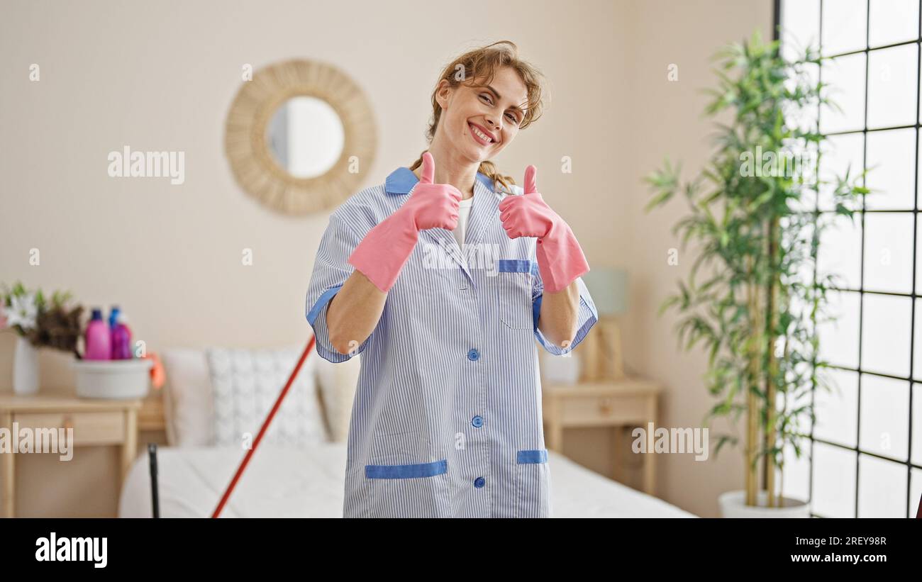 Young woman professional cleaner wearing gloves doing thumbs up gesture ...