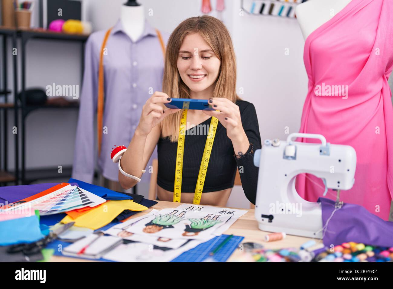 Young blonde woman tailor make photo by smartphone to clothing design ...