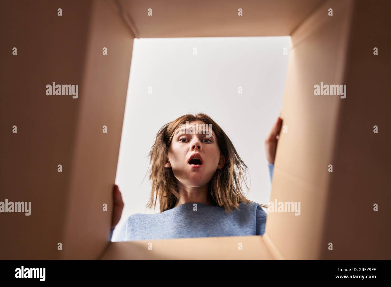 Beautiful woman opening cardboard box afraid and shocked with surprise ...