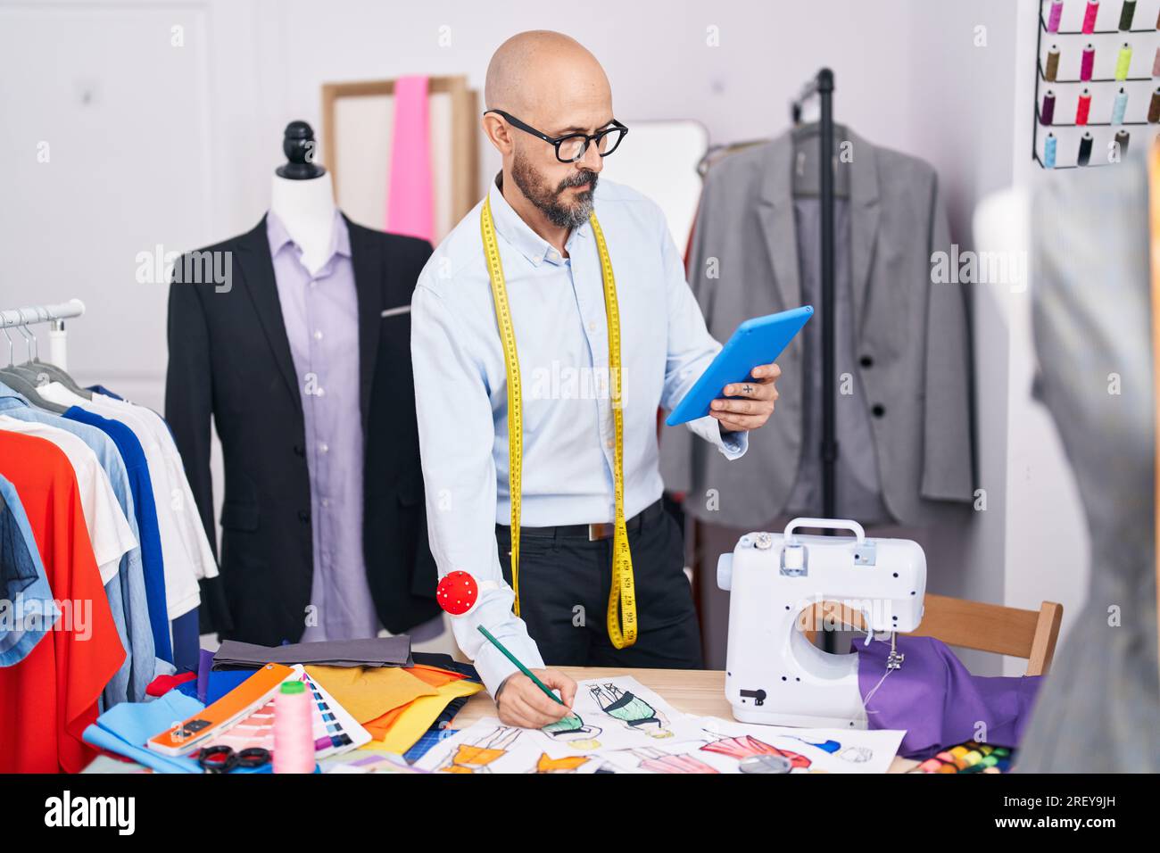 Young bald man tailor using touchpad drawing clothing design at tailor ...