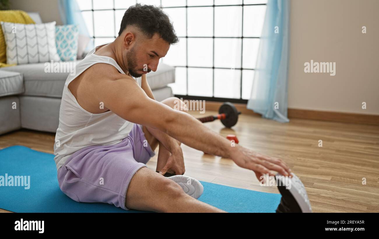 Young arab man stretching legs sitting on yoga mat at home Stock Photo ...