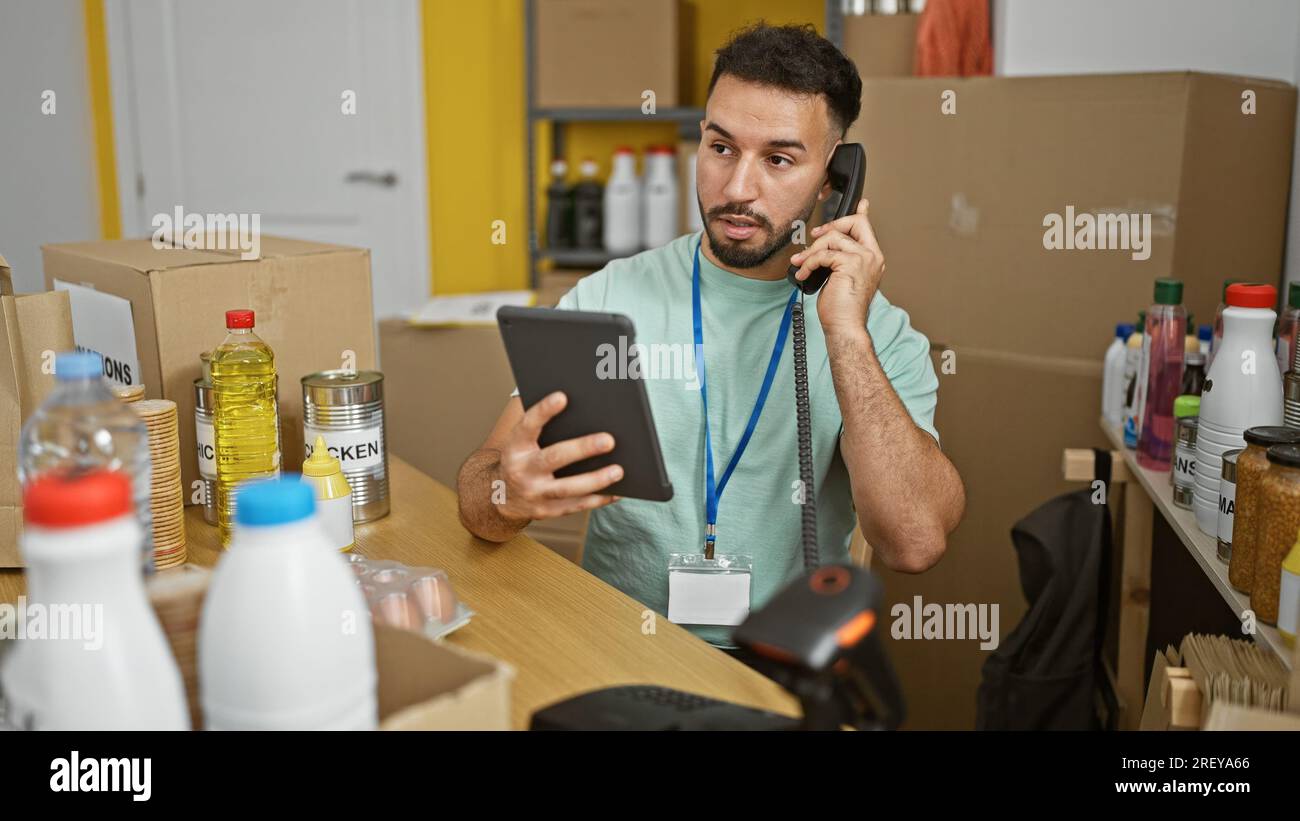 Young arab man volunteer using touchpad talking on telephone at charity ...
