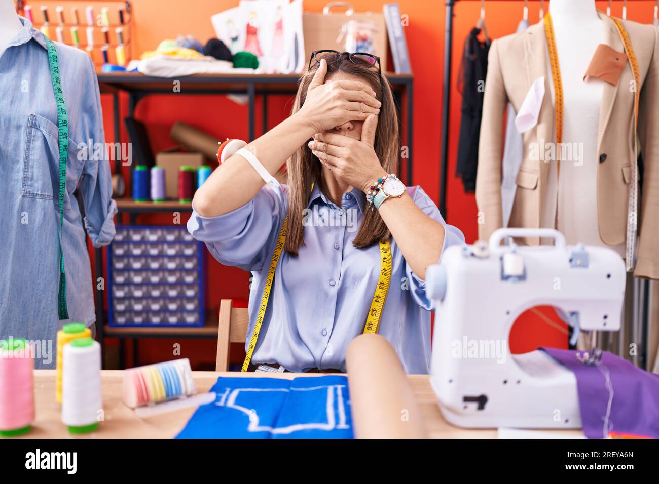 Hispanic young woman dressmaker designer at atelier room covering eyes ...