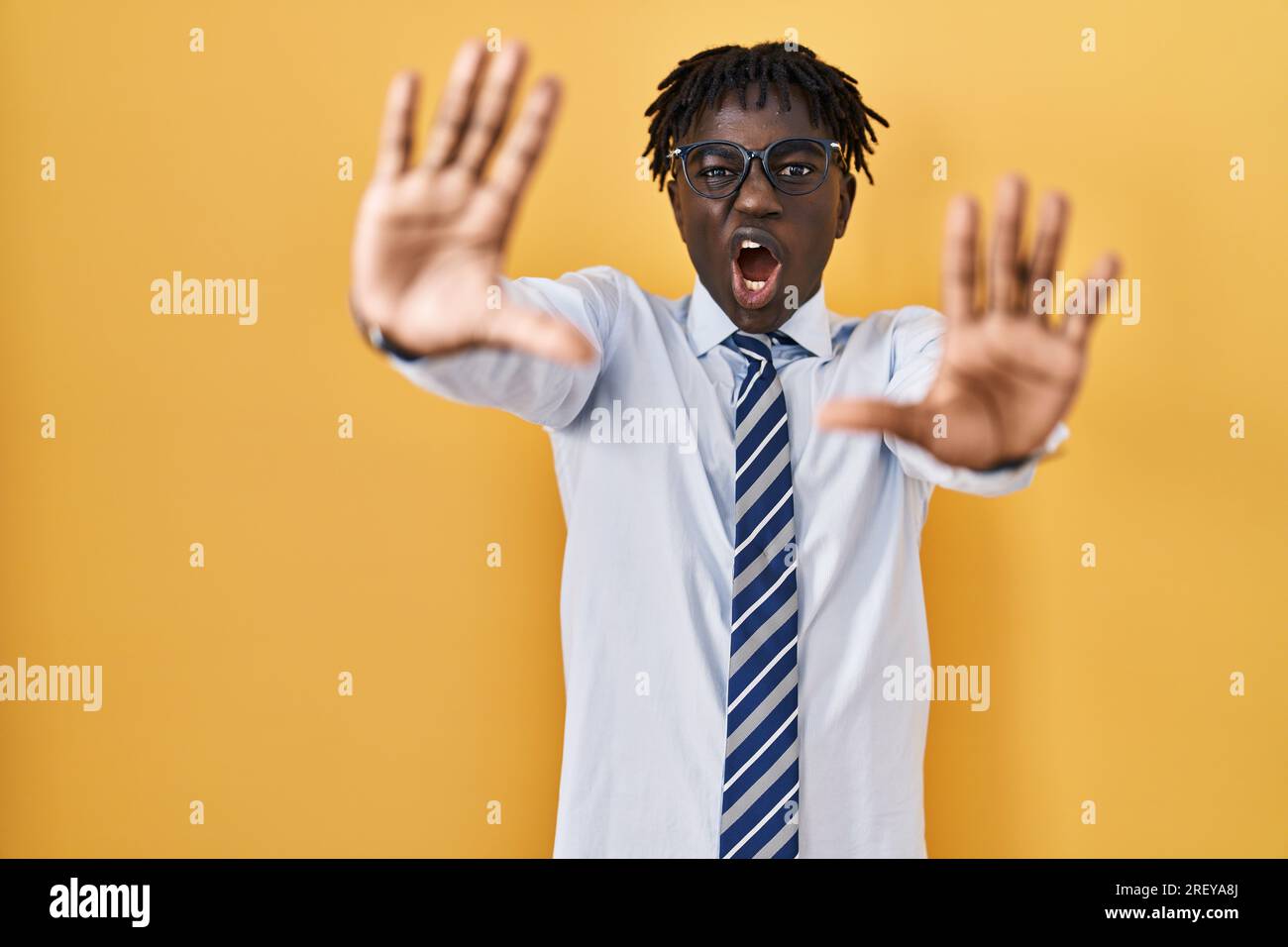 African man with dreadlocks standing over yellow background afraid and ...