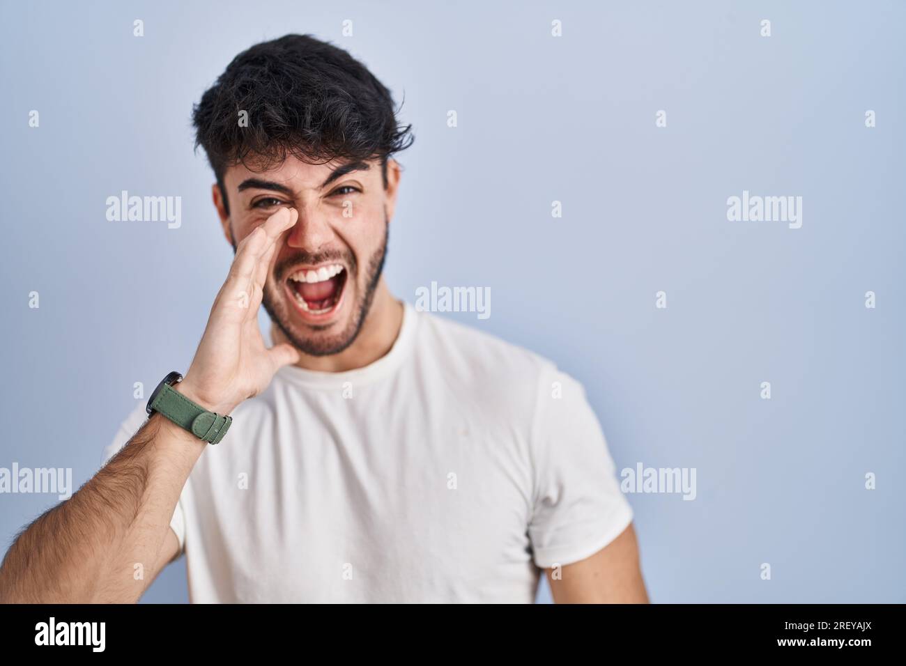 Hispanic man with beard standing over white background shouting and ...