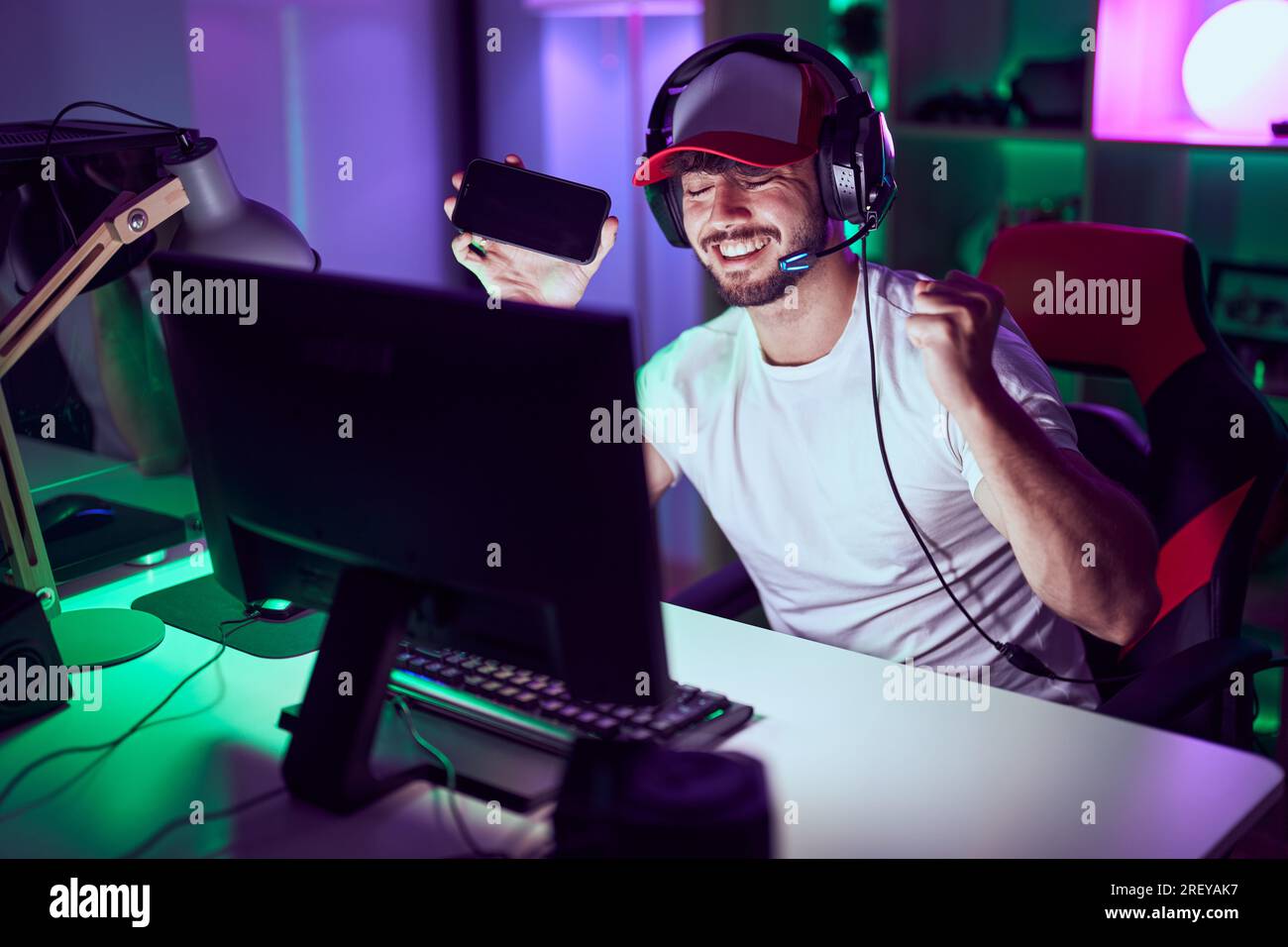 Hispanic man with beard playing video games with smartphone screaming ...