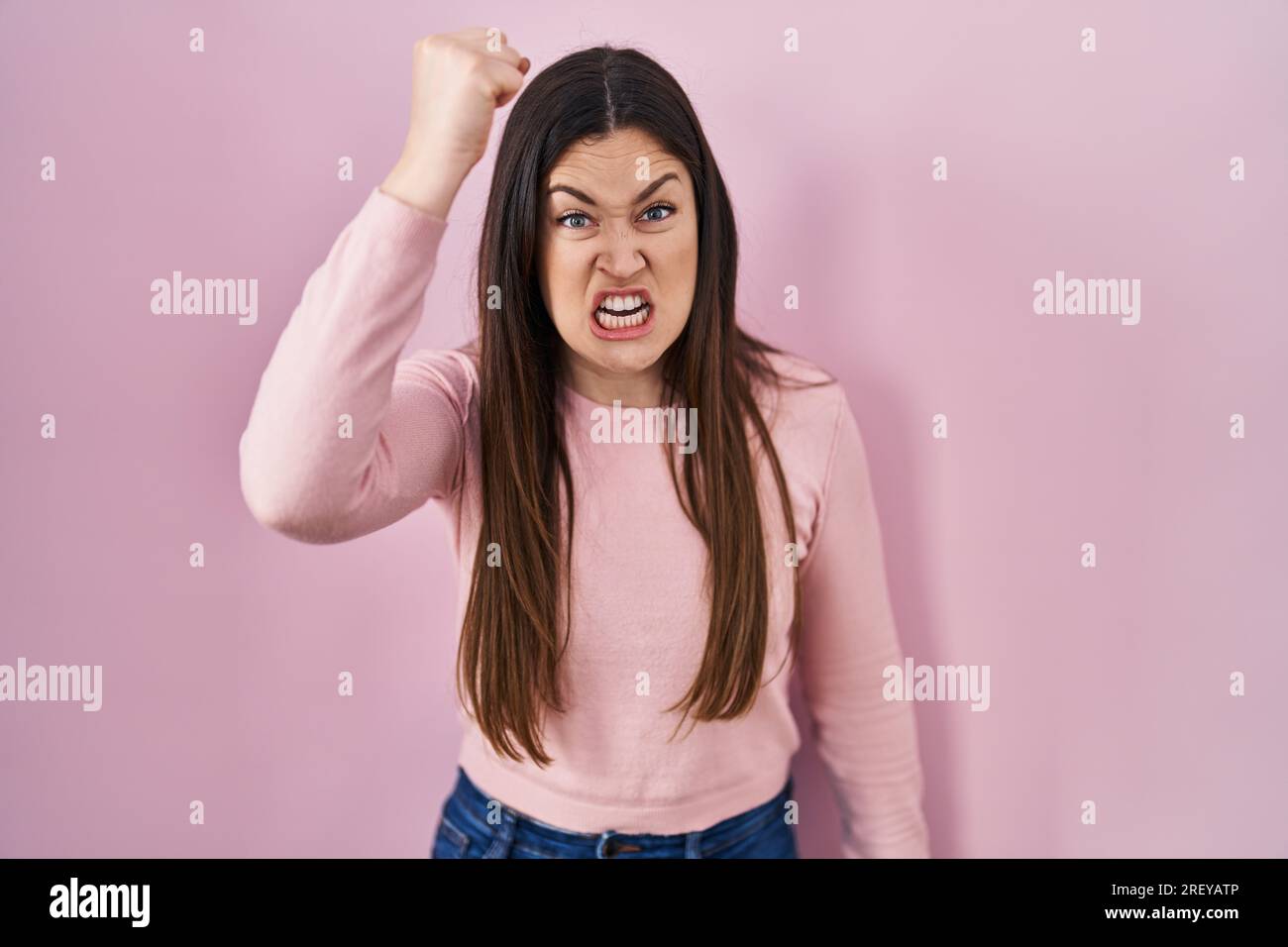 Young brunette woman standing over pink background angry and mad ...