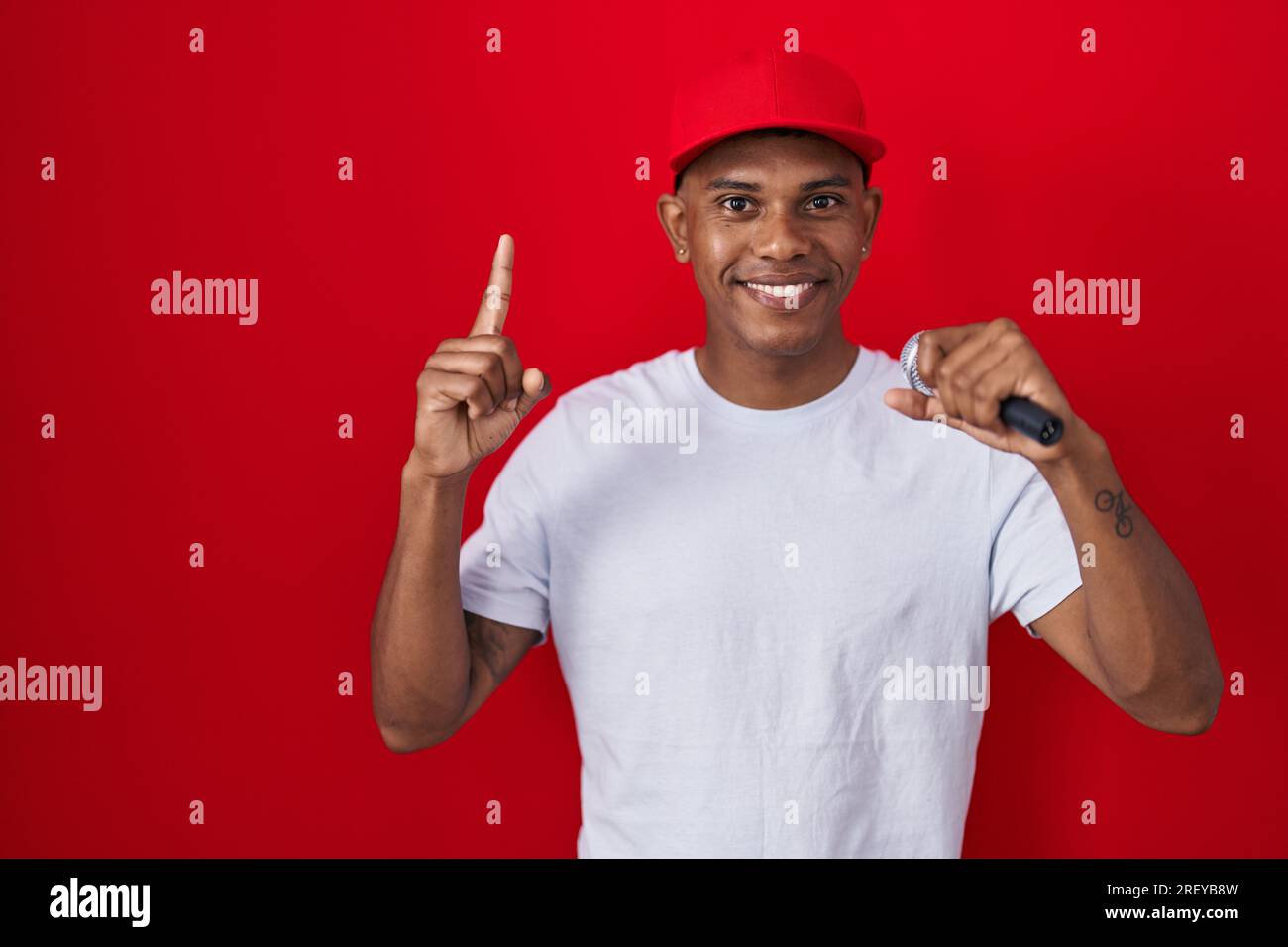 Young hispanic man singing song using microphone surprised with an idea ...