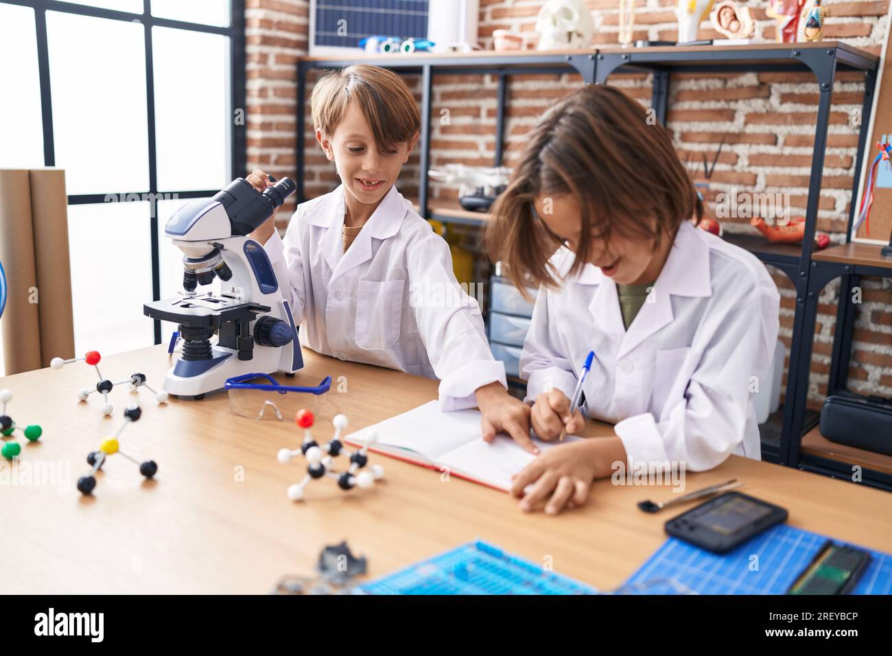 Adorable boys students using microscope writing notes at laboratory ...