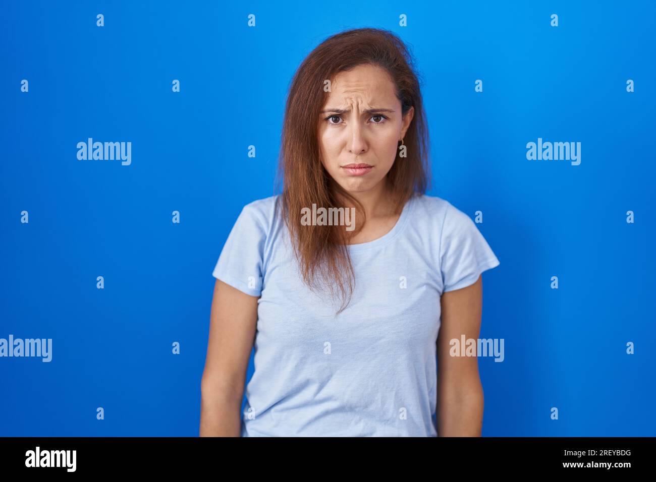 Brunette woman standing over blue background depressed and worry for ...