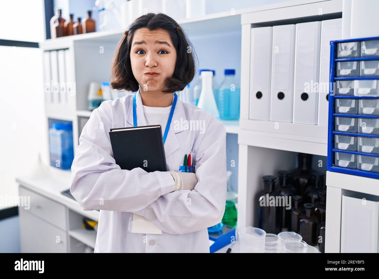 Young hispanic woman working at scientist laboratory puffing cheeks ...