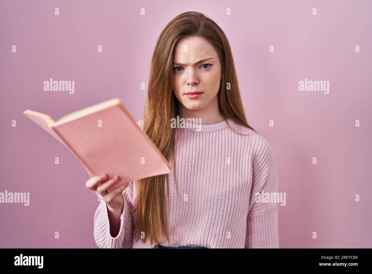 Young caucasian woman reading a book over pink background skeptic and ...