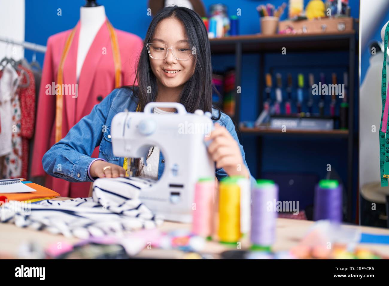 Young chinese woman tailor smiling confident using sewing machine at ...