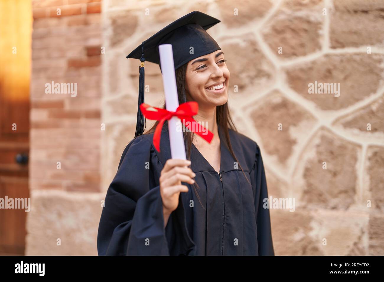 Young hispanic woman wearing graduated uniform holding diploma at ...