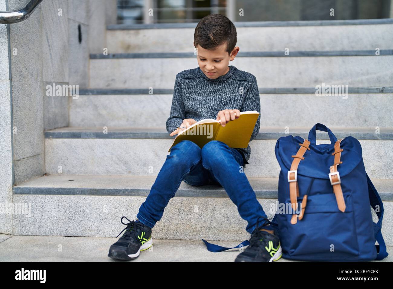 Blond child student writing on book sitting on stairs at school Stock ...