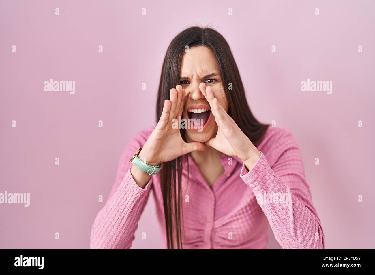 Young hispanic woman standing over pink background shouting angry out ...