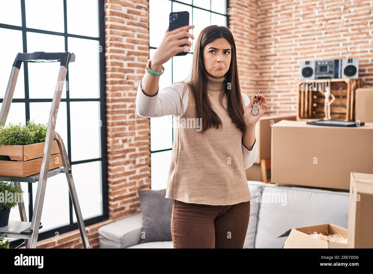 Young brunette woman moving to a new home doing video call depressed ...