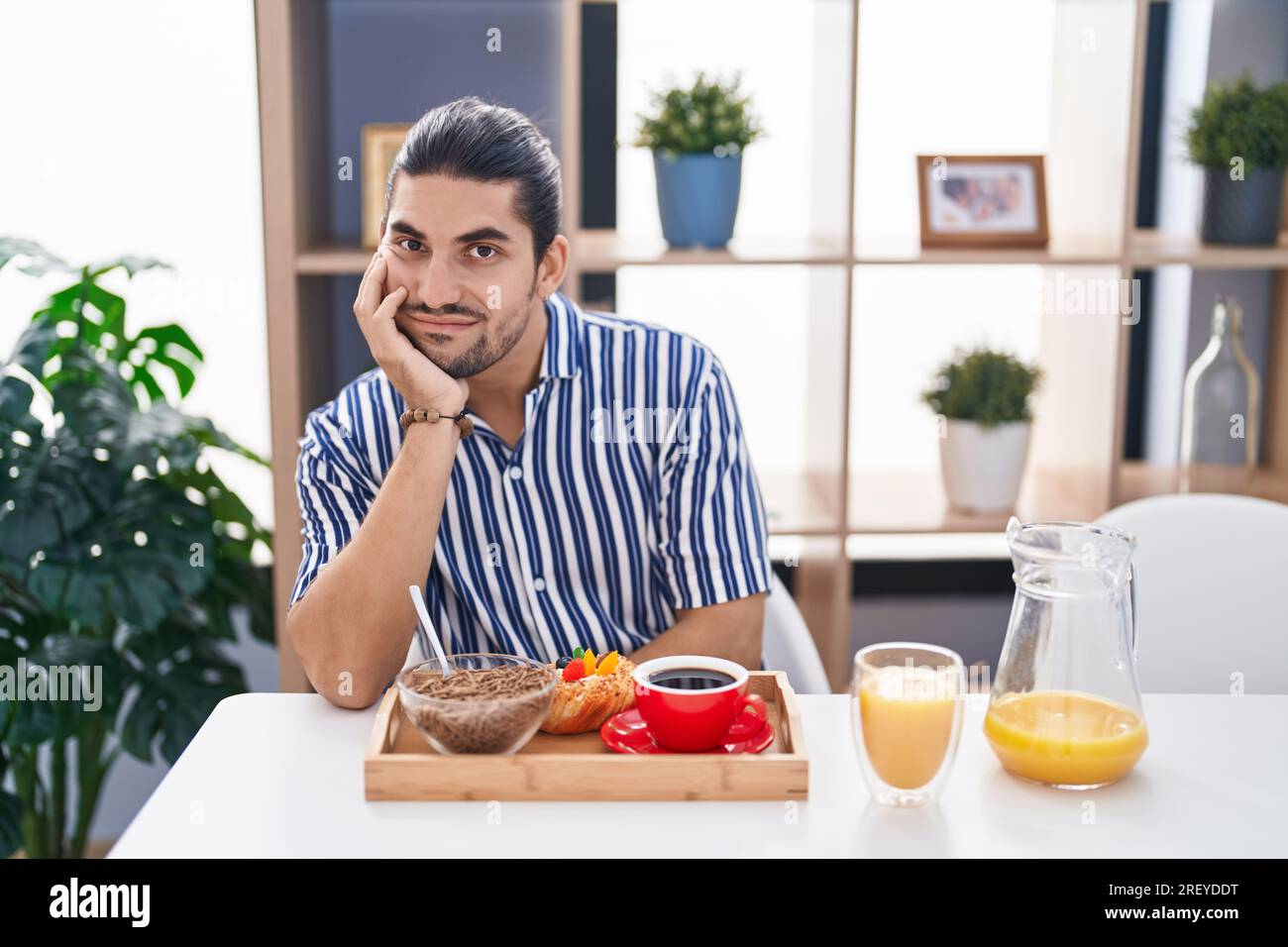 Hispanic man with long hair sitting on the table having breakfast ...